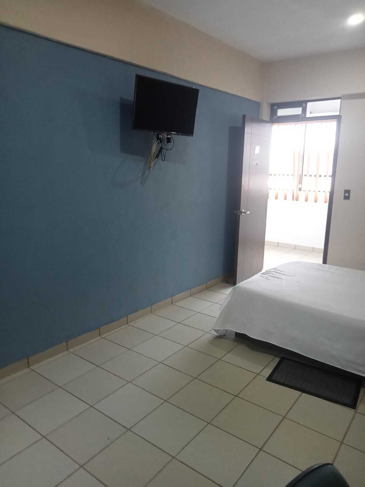 Quarto com cama, televisão fixada na parede e porta para área externa.
