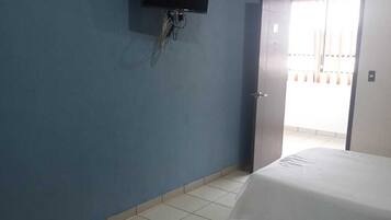 Quarto com cama, televisão fixada na parede e porta para área externa.