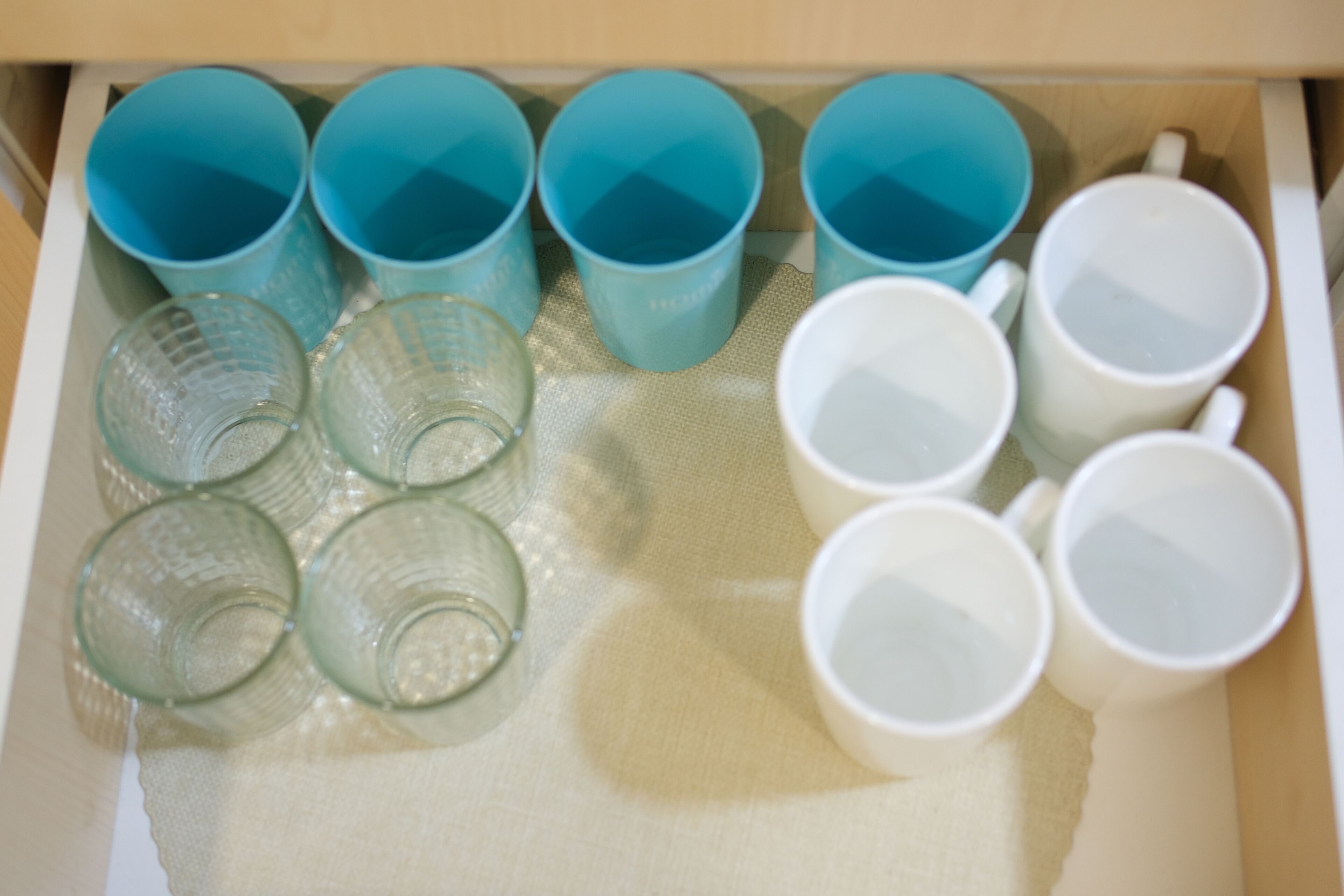 Uma gaveta com diversos utensílios de vidro, incluindo várias xícaras e copos azul e branco.