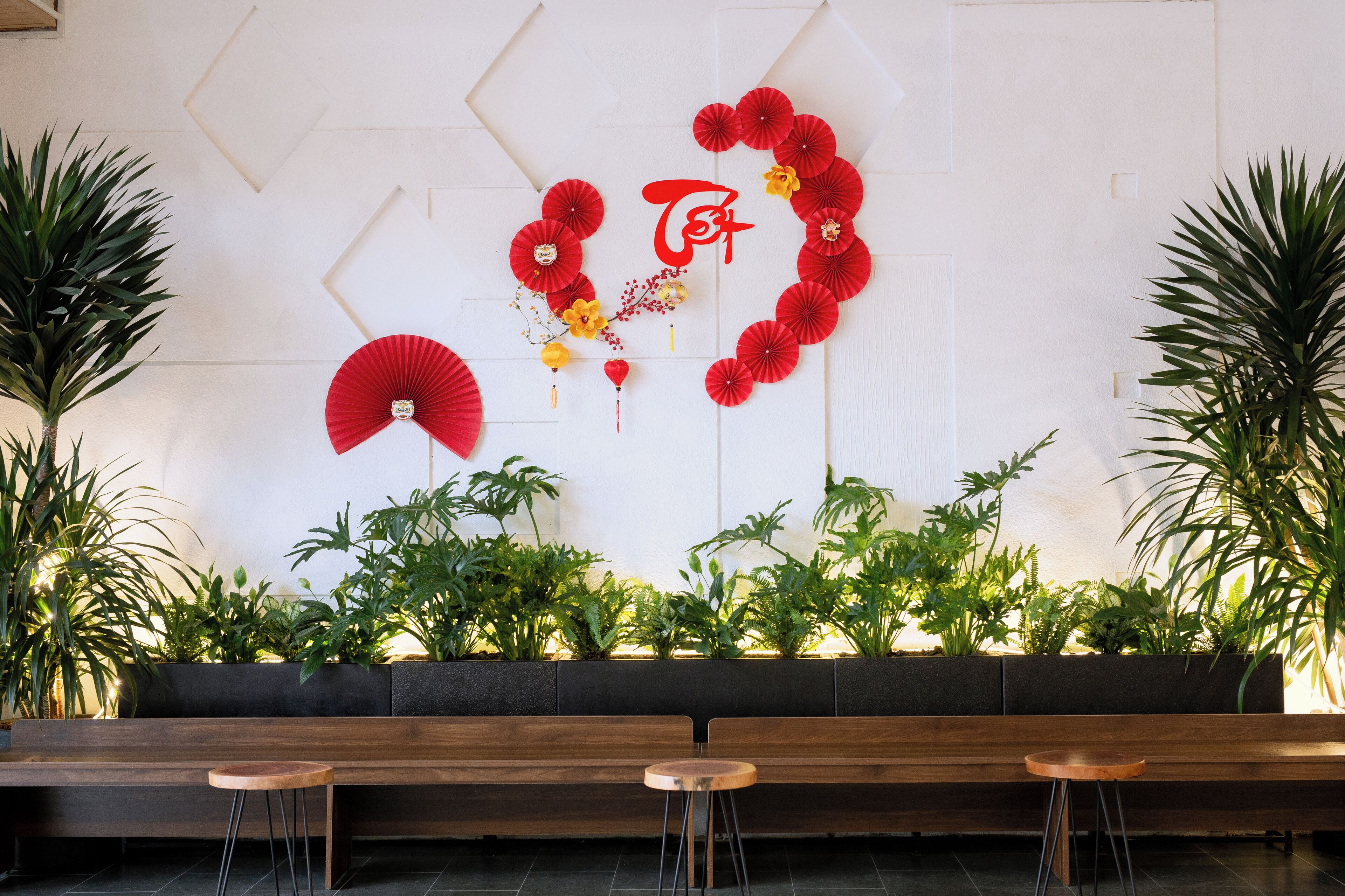 Uma área de recepção com um banco de madeira, uma pequena mesa redonda e uma parede decorada com leques de papel vermelhos e plantas.