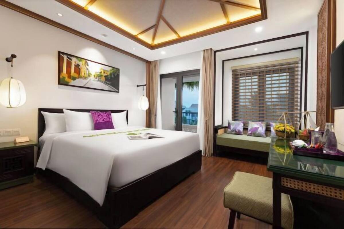 Quarto de hotel com uma cama grande, uma escrivaninha, uma cadeira, uma janela com persianas e um quadro na parede.