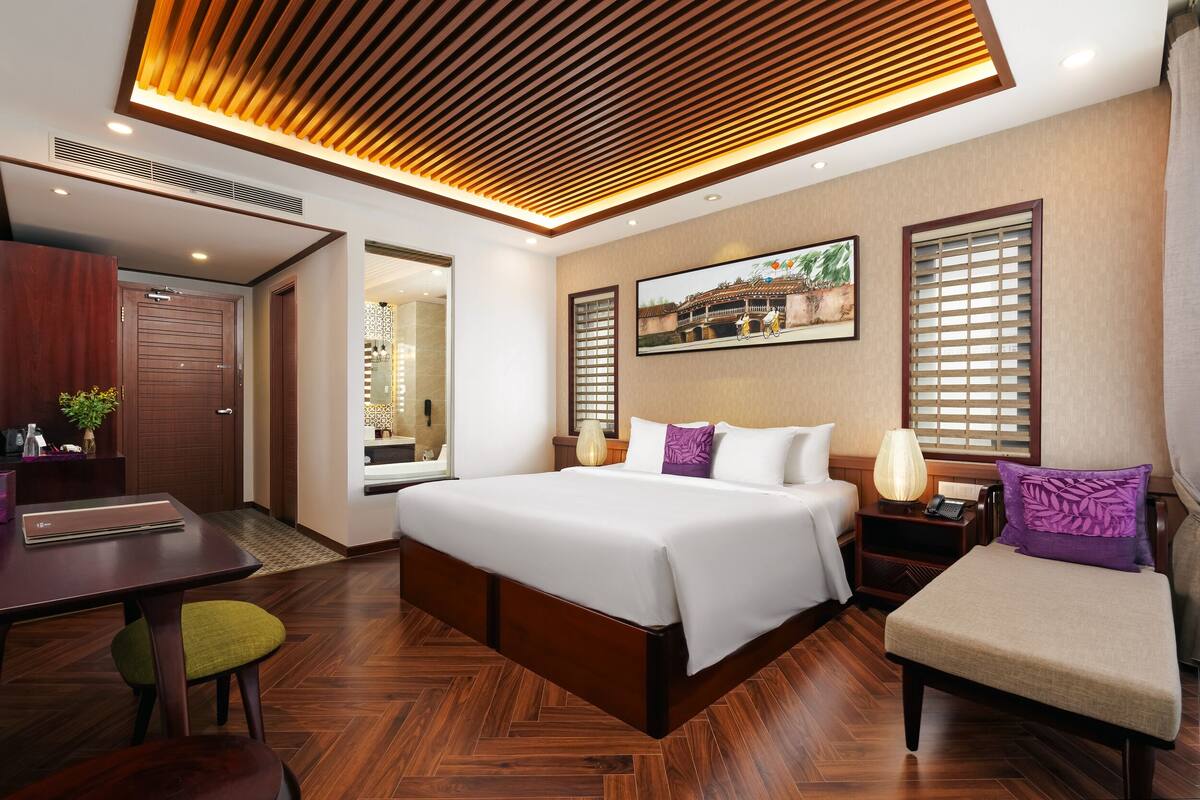 Quarto de hotel com uma cama grande, mesas de cabeceira, uma escrivaninha e uma cadeira.