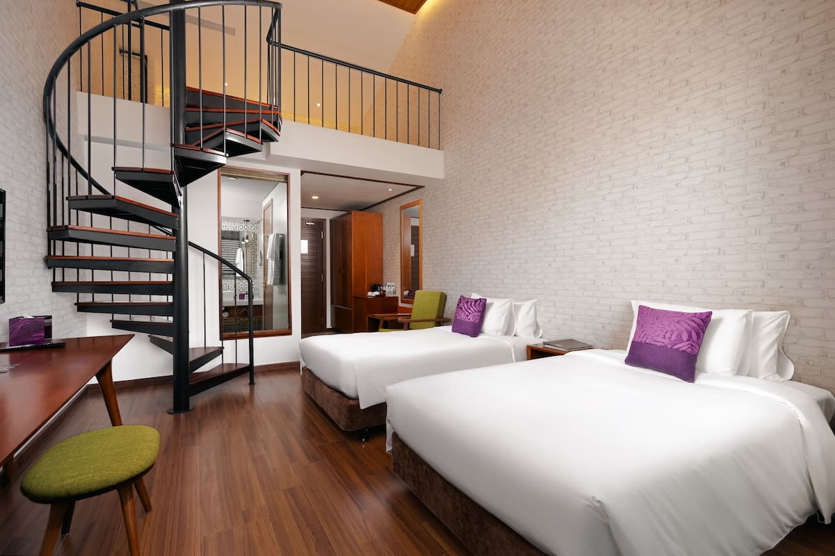 Quarto de hotel com escada em espiral, duas camas, uma escrivaninha e uma cadeira.
