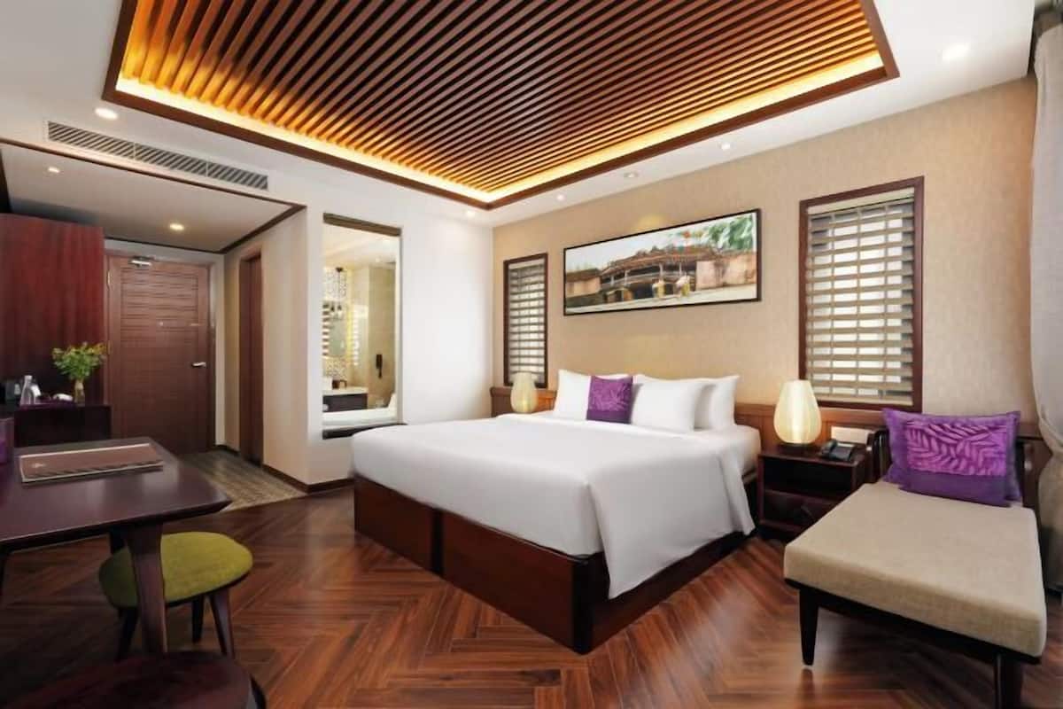Quarto de hotel com uma cama grande, mesas de cabeceira, escrivaninha e uma cadeira.