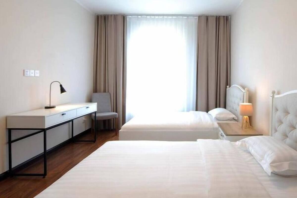 Quarto de hotel com cama, escrivaninha com luminária, cadeira e mesa de cabeceira com luminária.