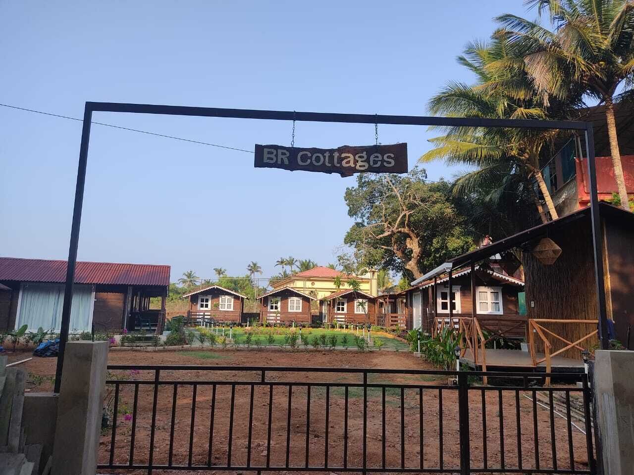 Entrada fechada para BR Cottages, com várias casas de madeira, um jardim cercado e céu claro.