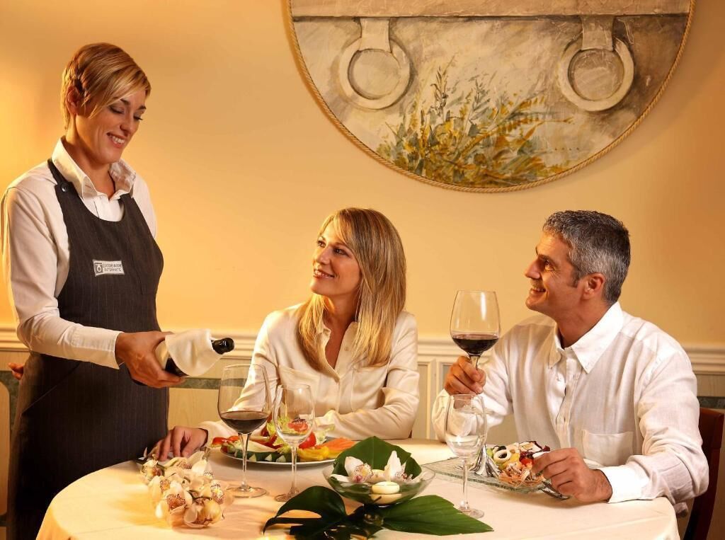 Uma mesa de jantar com um garçom servindo vinho a hóspedes.