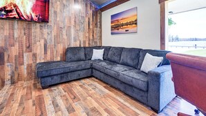 Uma sala de estar moderna com um sofá seccional, piso de madeira, televisão montada e um quadro na parede.