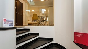 Escadaria que leva a um quarto com parede de vidro, uma cama e área de jantar com cadeiras e mesa.