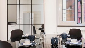 Uma sala de jantar moderna com uma mesa de vidro, cadeiras pretas e vista para o horizonte urbano pela janela.