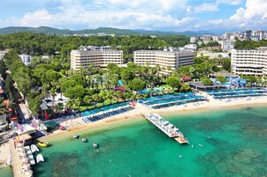 Um resort costeiro com vários edifícios de hotel, uma praia e um cais com barcos.