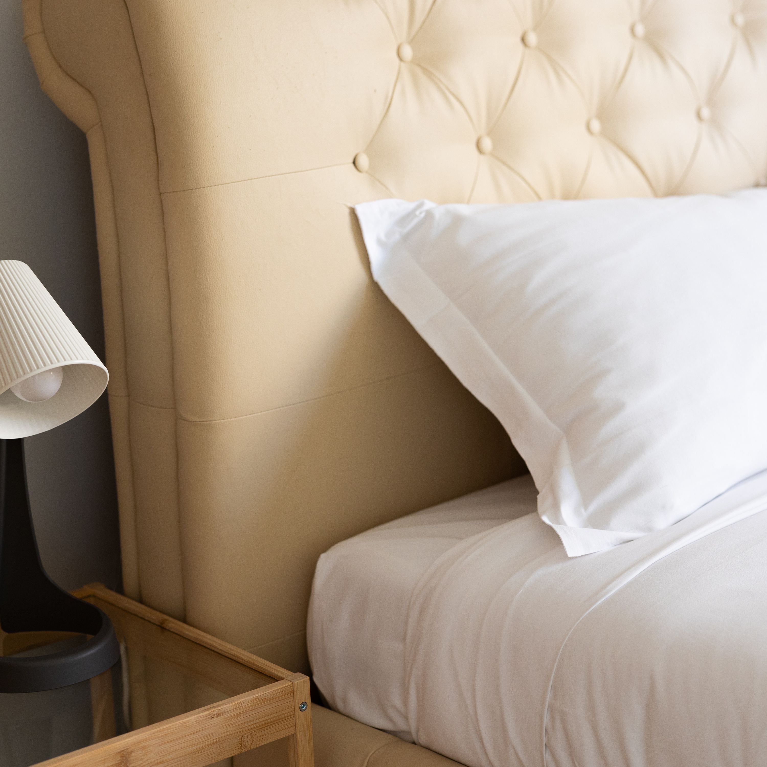 Uma cama com cabeceira estofada, luminária de cabeceira e mesa de cabeceira de madeira.