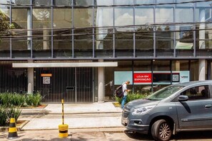 Um edifício moderno com fachada de vidro, uma placa indicando local de exportação e um carro estacionado na rua.