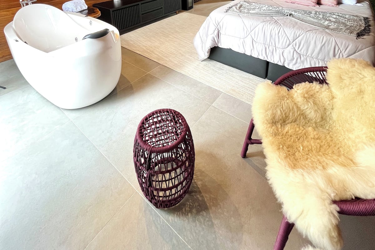 Quarto moderno com teto inclinado, uma cama grande, banheira branca, televisão e porta de vidro que dá para uma varanda.