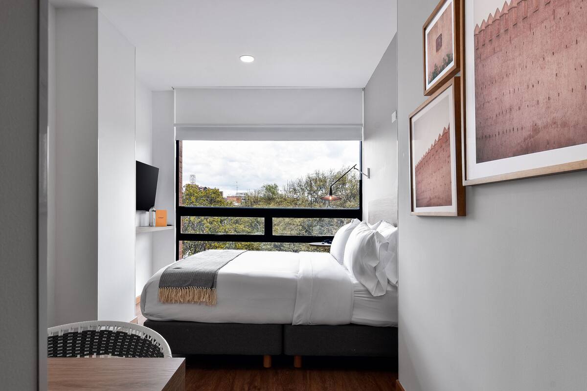Quarto moderno com cama, escrivaninha e janela com vista para a cidade.