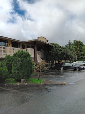 Um edifício com entrada coberta, estacionamento e uma fileira de árvores.