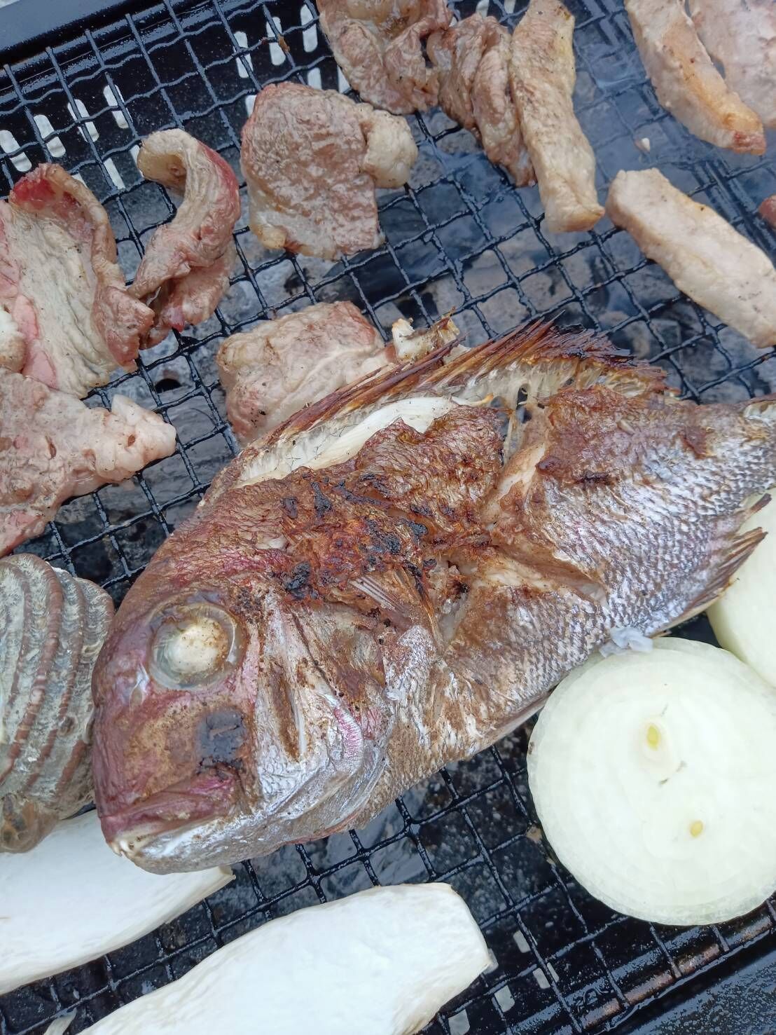 Peixe grelhado com pedaços de carne e cebola na grelha.