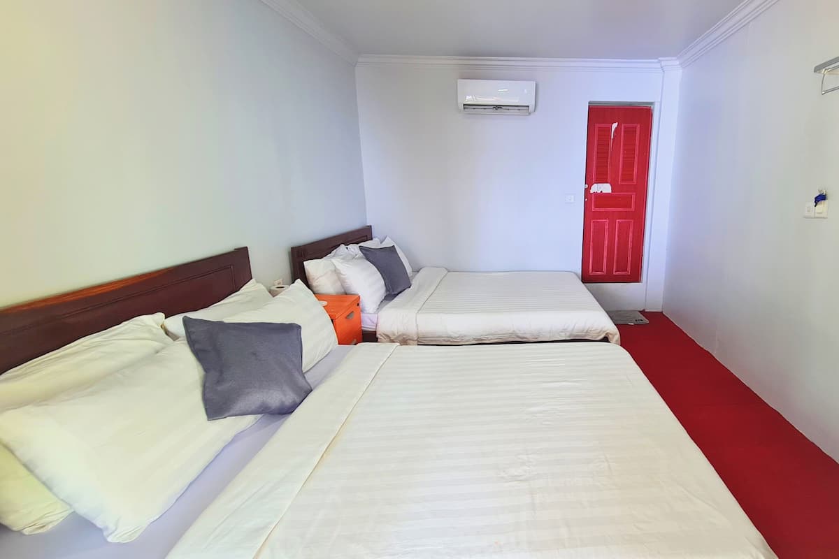 Quarto de hotel com duas camas, uma porta vermelha e um aparelho de ar condicionado na parede.