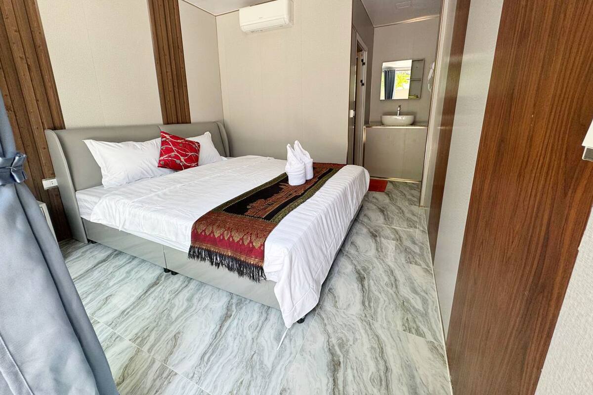 Quarto de hotel moderno com uma cama grande, banheiro com espelho e pia, e piso de madeira.