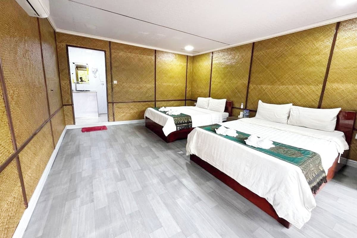 Quarto de hotel com duas camas, piso de madeira e parede com textura.