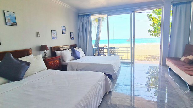Quarto de hotel com duas camas, um sofá e vista para a praia.