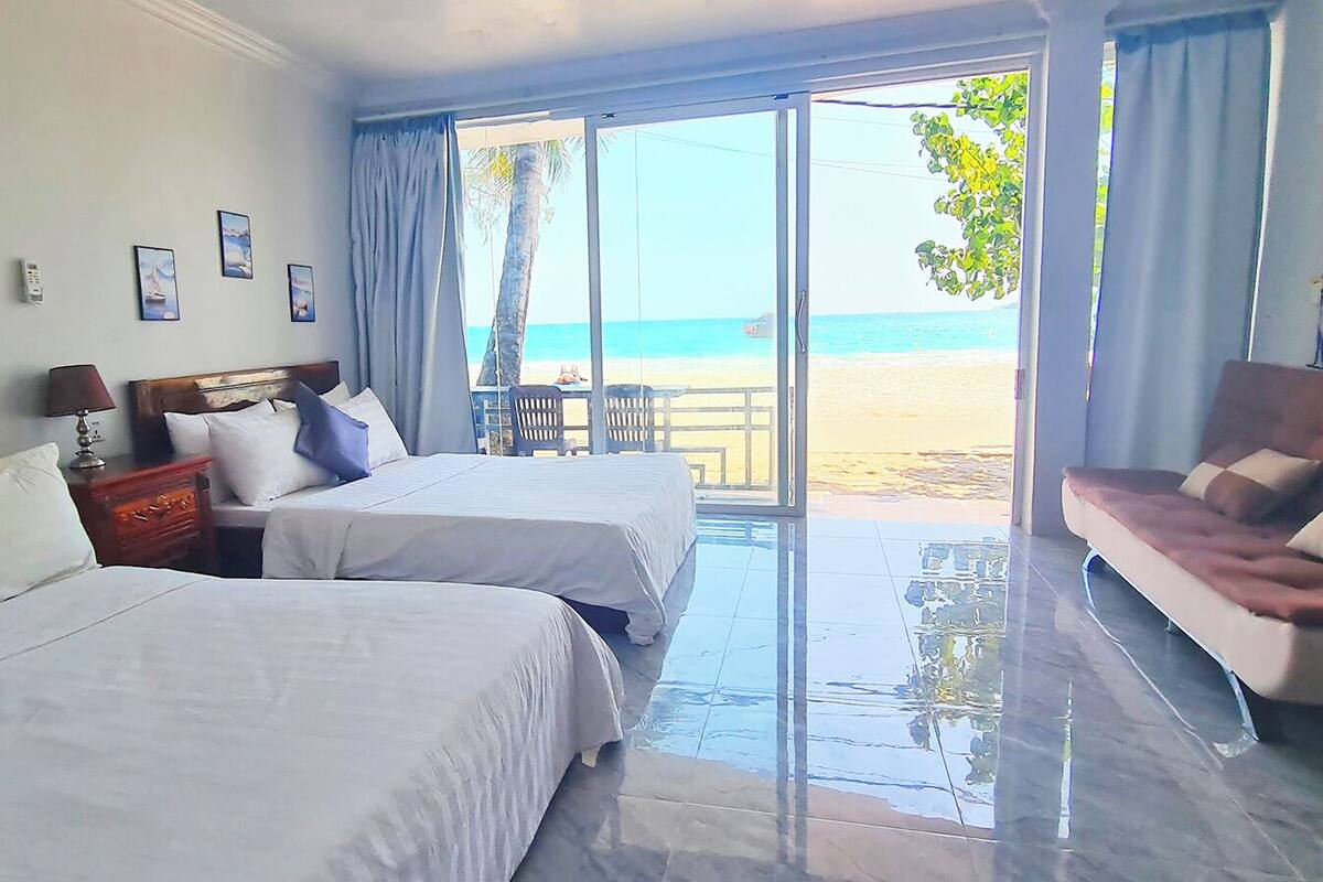 Quarto de hotel com duas camas, um sofá e vista para a praia.