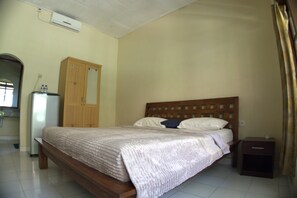 Quarto com cama de madeira, mesa de cabeceira pequena, guarda-roupa e frigorífico.