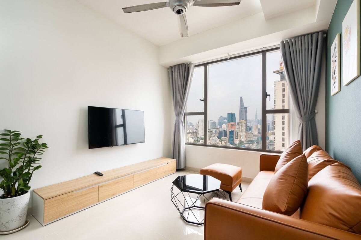 Uma sala de estar moderna com uma janela ampla, uma TV de tela plana, um sofá, uma mesa de centro e um vaso de planta.