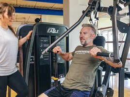 Uma academia com equipamento de exercícios, incluindo uma máquina de supino e uma máquina de remada sentada.