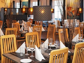 Interior de restaurante com cadeiras de madeira, mesas postas com guardanapos brancos, copos e talheres.