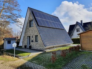 Uma casa moderna com telhado inclinado, painéis solares e um pequeno galpão.