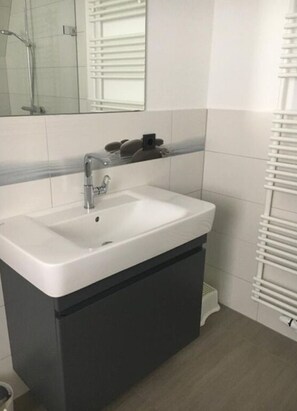 Casa de banho com lavatório branco, armário escuro e porta-toalhas.