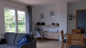 Uma sala de estar com sofá, mesa de jantar com cadeiras, televisão e estante de livros.