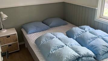 Uma cama de solteiro com roupa de cama e almofadas azuis, uma luminária de cabeceira e uma pequena cesta de vime sobre a mesinha de cabeceira.
