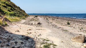 Trilho costeiro com terreno rochoso e vista para o mar.