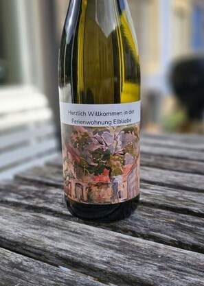 Uma garrafa de vinho com etiqueta que apresenta uma pintura de um edifício e árvores.