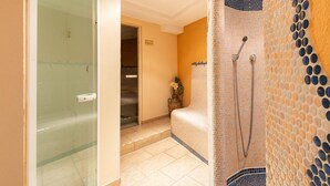 Casa de banho com porta de vidro, chuveiro com azulejos de mosaico e um sinal a indicar 