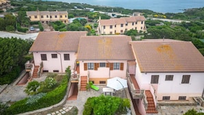 Uma área residencial costeira com casas de telhado em terracota, uma piscina e vista para o mar.
