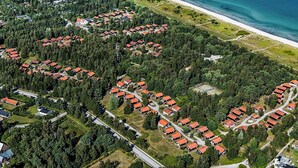 Vista aérea de uma área residencial costeira, com conjuntos de casas rodeadas por florestas densas, uma praia e um mar azul límpido.