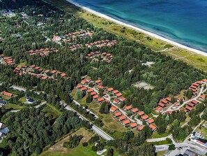 Vista aérea de uma área residencial costeira, com conjuntos de casas rodeadas por florestas densas, uma praia e um mar azul límpido.