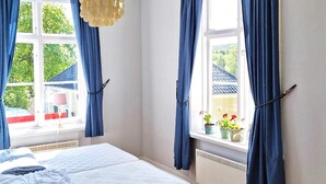Quarto com cama, janela com cortinas, luminária pendente e radiador.