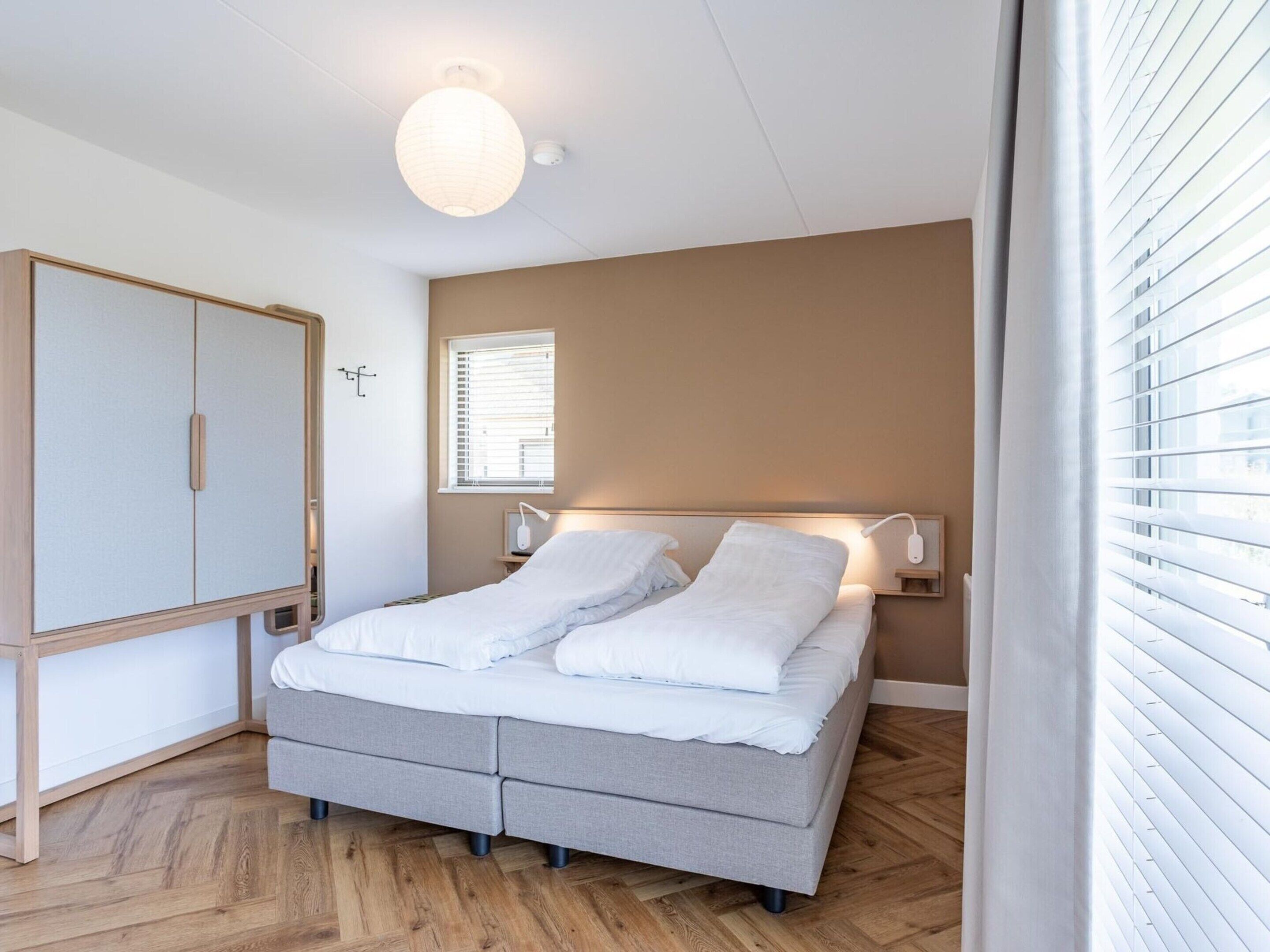 Quarto com cama, mesas de cabeceira, guarda-roupa e janela com persianas.