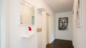 Corredor com toucador branco, espelho, flor vermelha e obra de arte na parede.