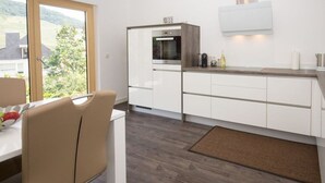 Uma cozinha moderna com armários brancos, forno embutido e vista para uma paisagem verde através de uma janela ampla.