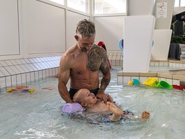 Um homem em uma piscina com uma criança, cercado por diversos brinquedos de piscina.
