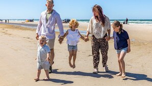 Uma família caminhando numa praia de areia, com o oceano ao fundo.