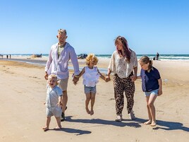 Uma família caminhando numa praia de areia, com o oceano ao fundo.