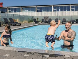 Piscina com cadeiras de praia e um edifício ao fundo.
