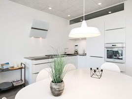 Uma cozinha moderna com armários brancos, uma ilha central, forno embutido e uma luminária pendente.