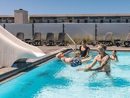 Piscina com escorregador, espreguiçadeiras e um edifício ao fundo.